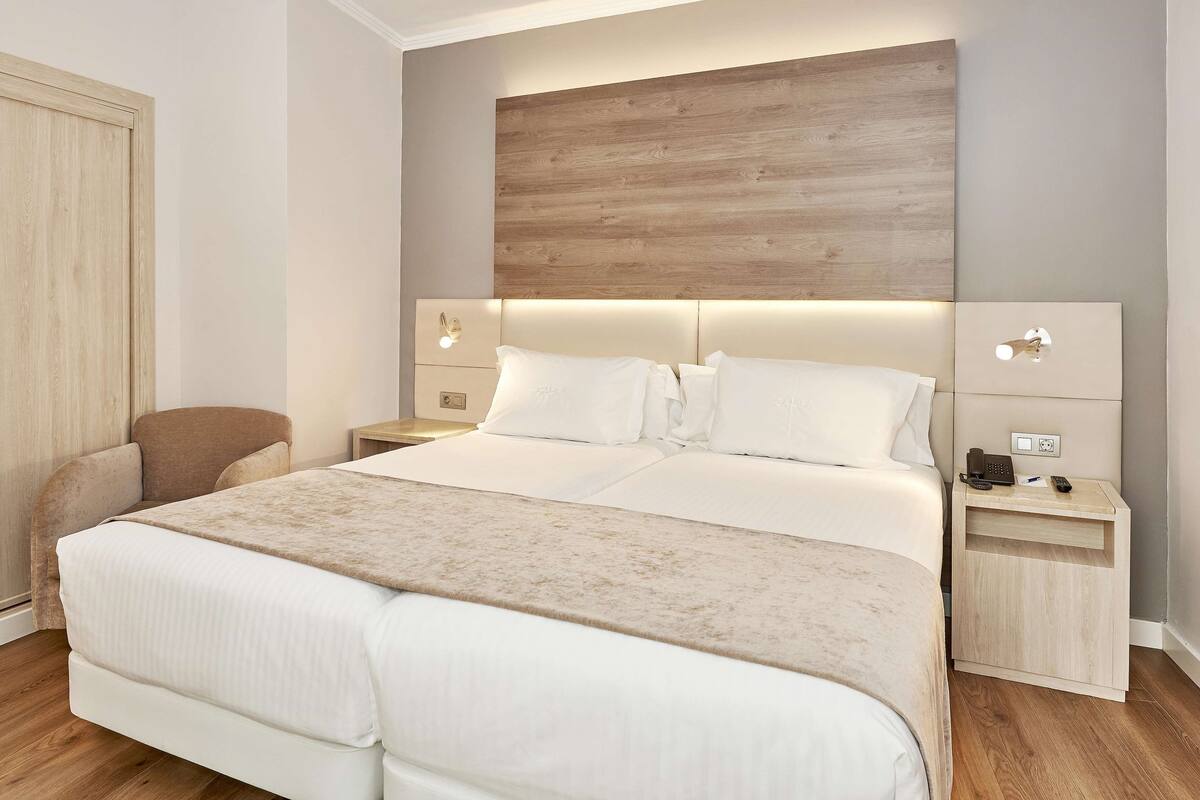 Quarto moderno com uma cama grande, mesas de cabeceira, uma cadeira e um guarda-roupa.