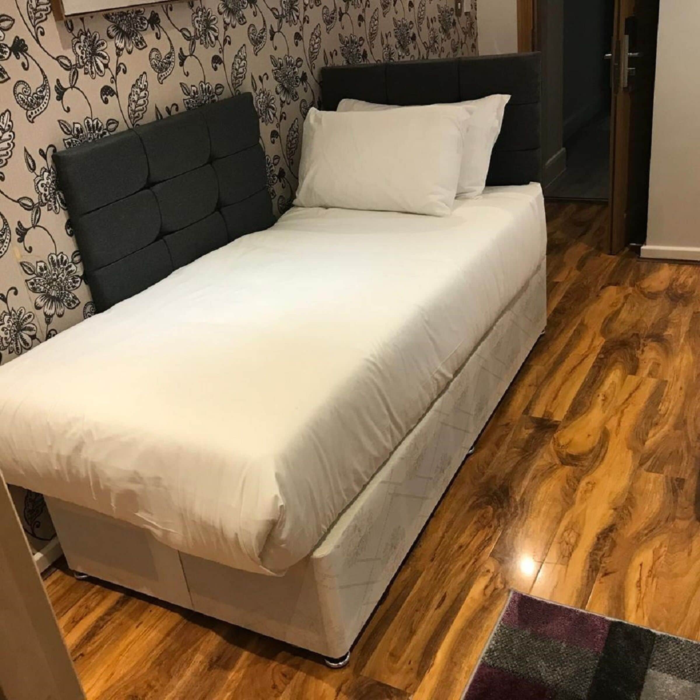 Quarto com cama, cabeceira escura e papel de parede com padrão floral.