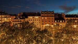 Vista noturna de uma fileira de edifícios altos com janelas iluminadas, cercados por árvores.