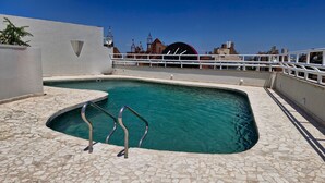 Piscina no terraço com deck de ladrilho de pedra e grades de metal.