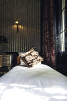 Quarto de hotel com cama, mesa de cabeceira, abajur e cortinas.