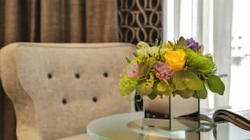 Mesa de vidro com um arranjo floral numa sala com sofá estofado e parede estampada.