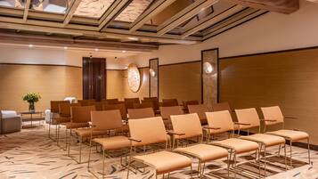 Uma sala de conferências com fileiras de cadeiras, parede de painéis de madeira, relógio e teto com claraboias.