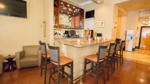 Uma área de bar com balcão, banquetas, televisão e frigorífico.
