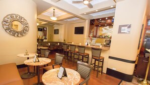 Restaurante com mesas redondas, assentos acolchoados, área de bar e ventilador de teto.