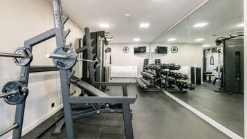 Academia com equipamentos de musculação, espelhos e quadro branco.