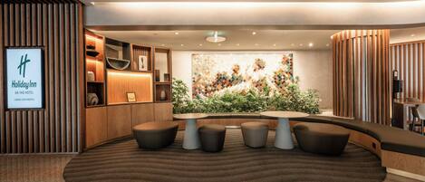 Um saguão de hotel moderno, com uma área de estar circular, detalhes em madeira e um grande painel decorativo.