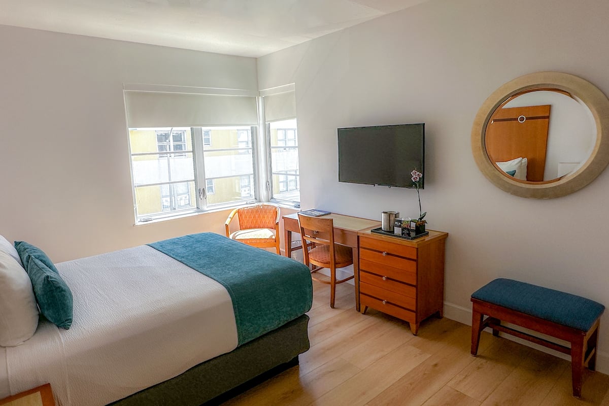 Quarto com cama, escrivaninha, cadeira e televisão.