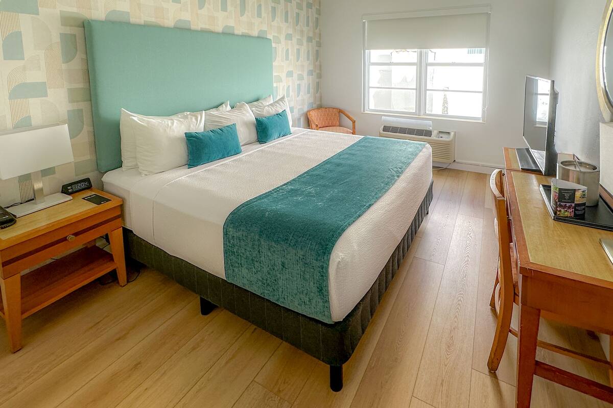 Quarto de hotel com uma cama, mesas de cabeceira de madeira, uma escrivaninha e uma cadeira.