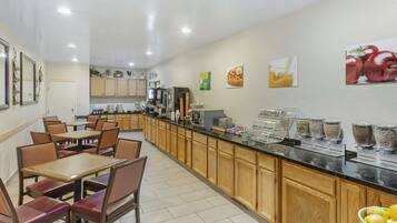 Espaço de café da manhã com armários de madeira, balcão longo com diversos alimentos e assentos com cadeiras estofadas.