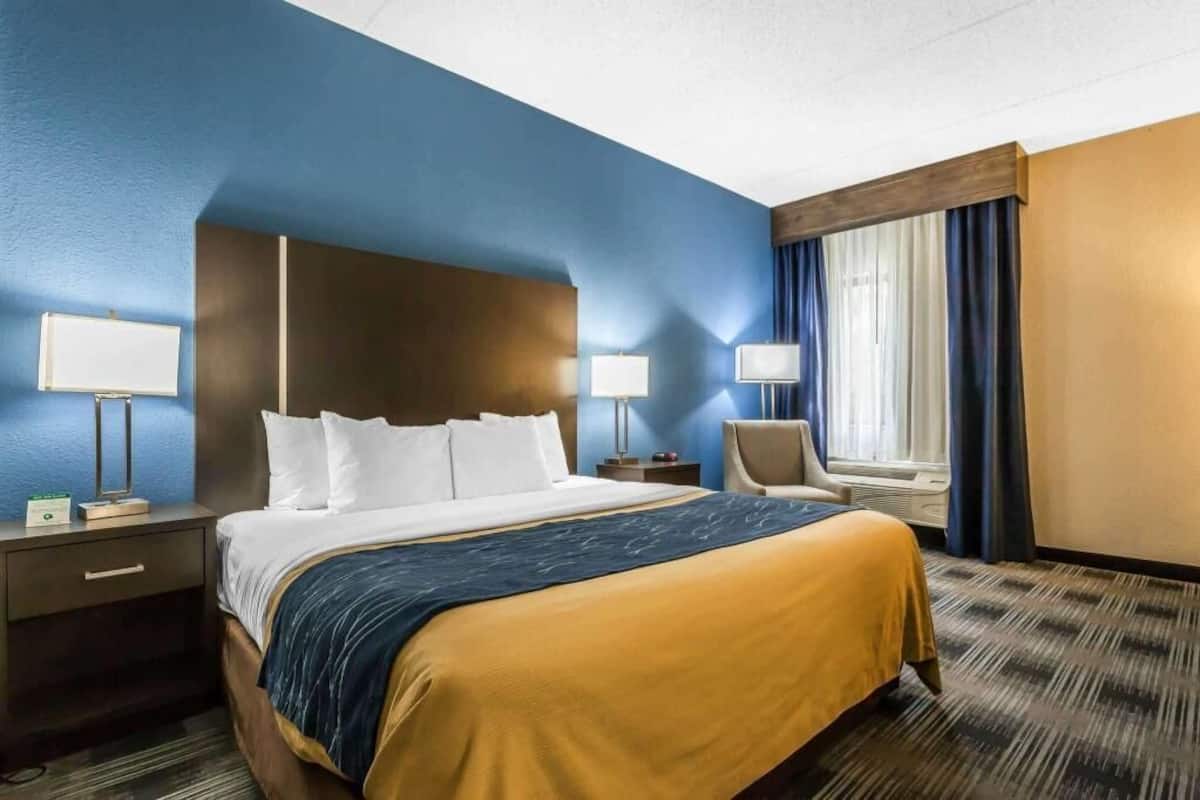 Quarto de hotel com uma cama grande, duas mesas de cabeceira, uma cadeira e uma janela com cortinas.