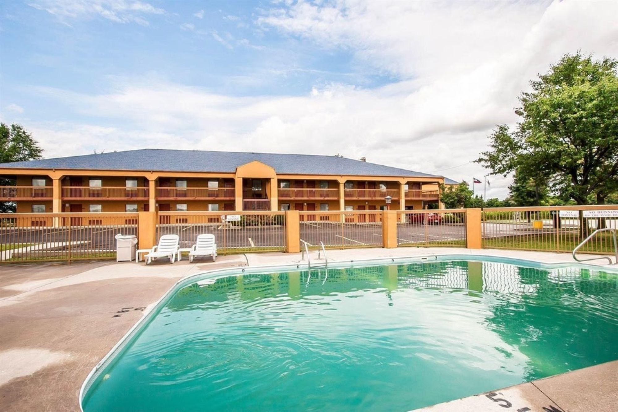 Um motel com piscina, área de estar externa e estacionamento cercado.