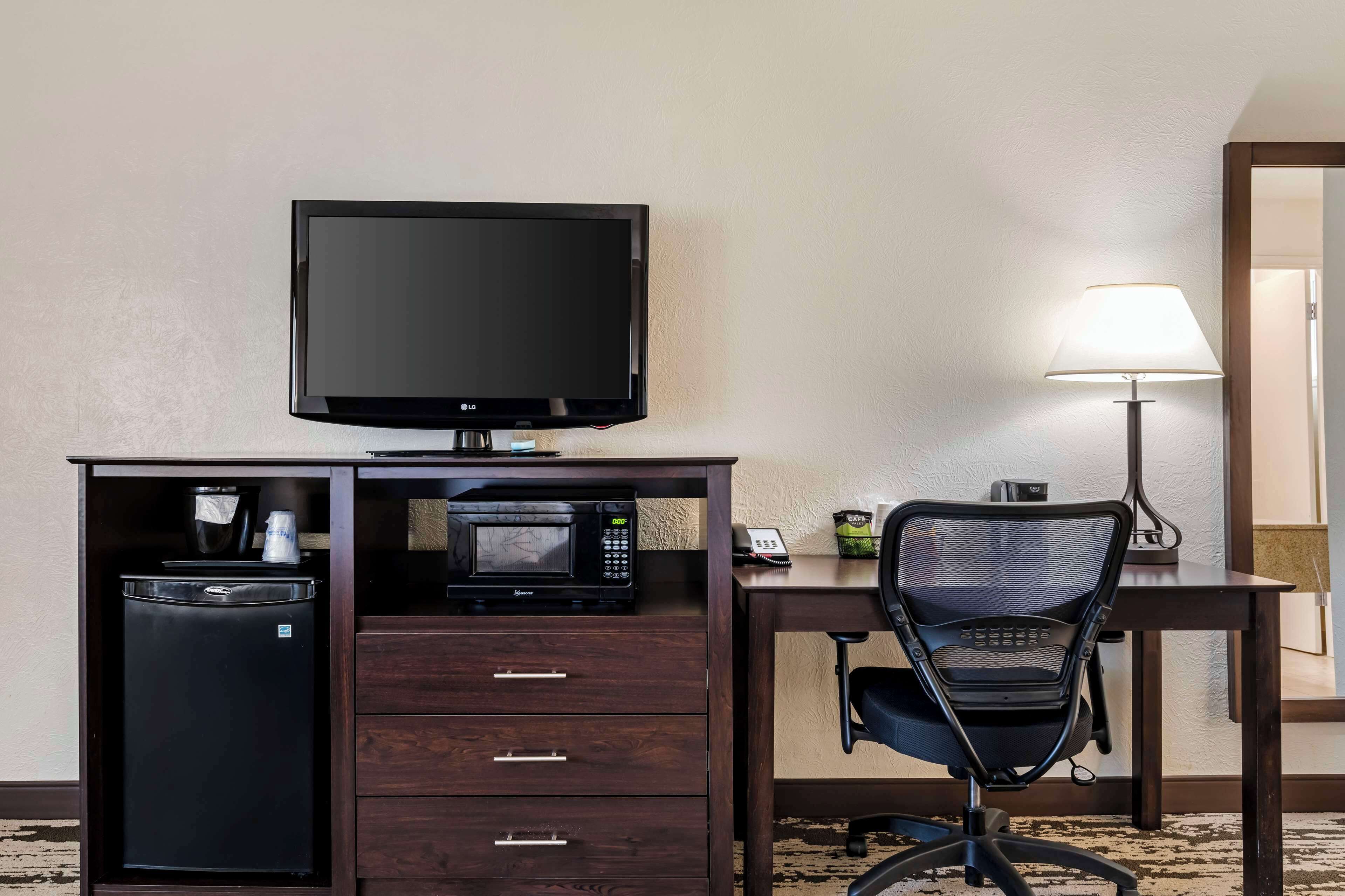 Quarto de hotel com televisão de tela plana, micro-ondas, mini-geladeira, escrivaninha com cadeira e luminária.