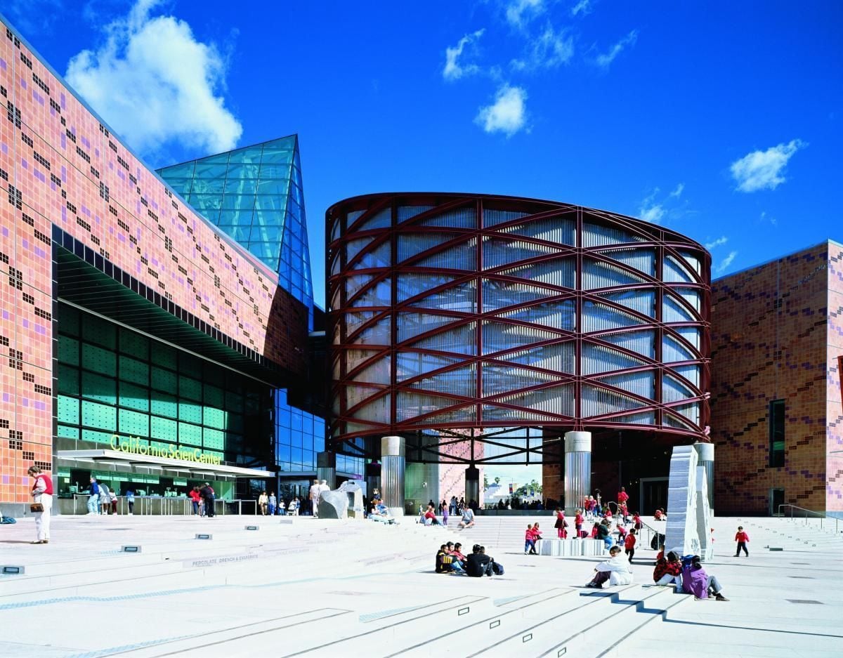 Um edifício moderno com fachada de vidro e estrutura metálica vermelha marcante.