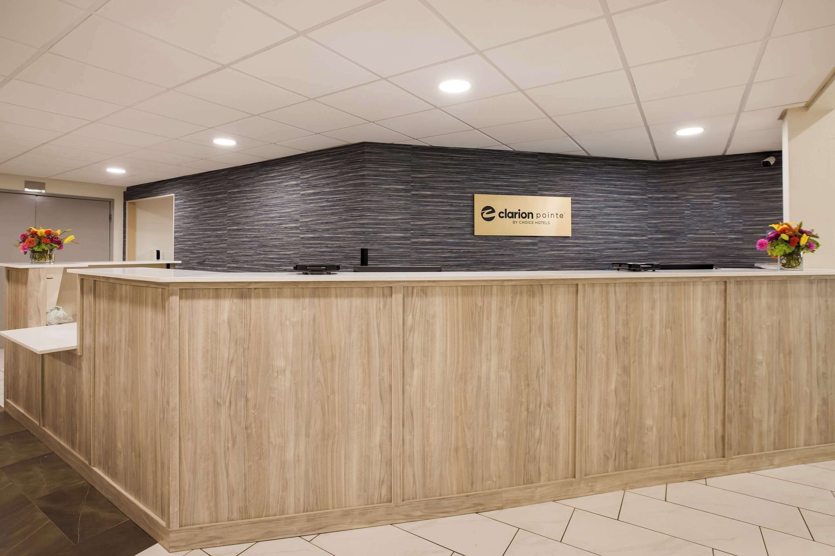 Uma receção com acabamento em madeira, parede escura com textura e um sinal para 'Clarion Point by Choice Hotels'.