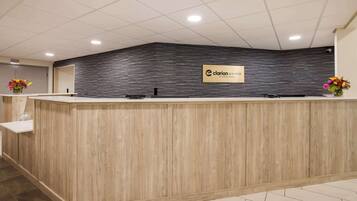 Uma receção com acabamento em madeira, parede escura com textura e um sinal para 'Clarion Point by Choice Hotels'.