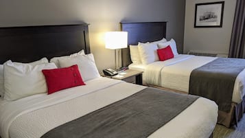 Quarto de hotel com duas camas, cada uma com roupa de cama branca e almofadas vermelhas, uma mesa de cabeceira com abajur e um quadro na parede.
