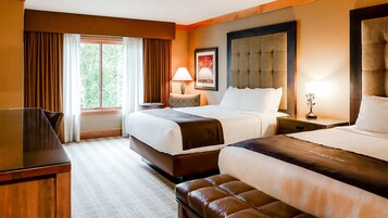 Quarto de hotel com duas camas, uma escrivaninha e uma janela grande com cortinas.