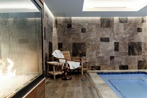 Uma área de spa com parede de pedra, piscina e cadeiras de madeira.