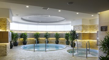 Uma área de spa com uma banheira de hidromassagem circular, paredes de pedra e plantas em vasos.