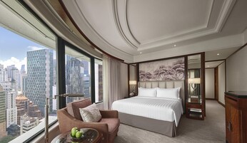 Quarto de hotel com uma cama grande, um sofá, uma mesa com maçãs e vista para a cidade.