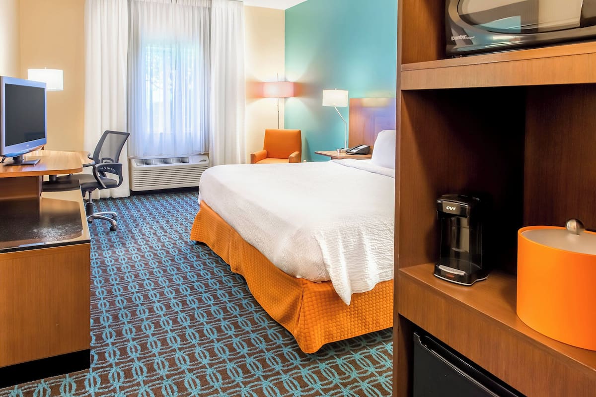 Quarto de hotel com cama, escrivaninha, cadeira, ar condicionado, luminárias e cafeteira.