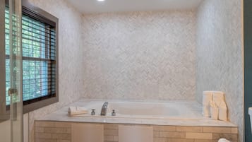 Uma casa de banho com uma banheira grande, uma janela com persianas e uma parede revestida a azulejos.