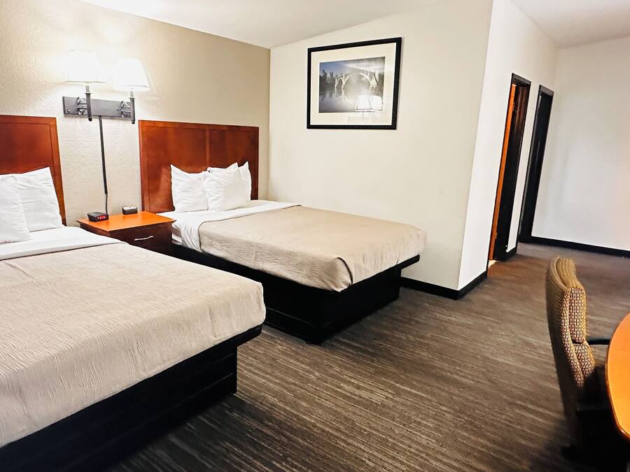 Quarto de hotel com duas camas, uma escrivaninha, uma cadeira, um abajur e um quadro na parede.