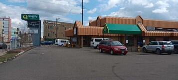 Um estacionamento com uma placa da Quality Inn, um prédio da Habitat for Humanity, e um carro vermelho estacionado na frente.