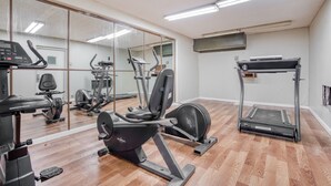 Uma academia com máquinas de cardio, equipamentos de peso e um espelho grande.