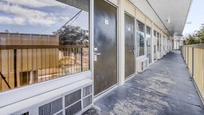 Corredor com portas numeradas 210, janelas amplas e grade de metal.