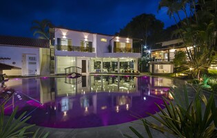Uma casa moderna de dois andares com piscina, grandes janelas e iluminação externa.