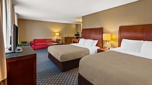 Quarto de hotel com duas camas, uma escrivaninha, televisão, sofá vermelho e uma pequena copa.