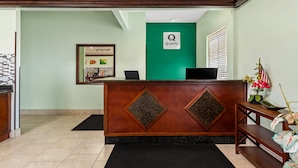 Uma área de recepção com parede verde, balcão de madeira e um cardápio emoldurado na parede.