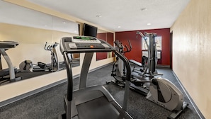 Uma academia com máquinas de cardio, equipamentos de musculação e um espelho grande.
