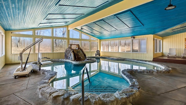 Uma grande piscina interior com uma cascata de pedra, rodeada por amplas janelas e um teto alto com claraboias.