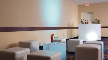 Um saguão de hotel com área de bar, assentos e piso coberto por carpete.