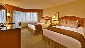 Quarto de hotel com duas camas, uma escrivaninha, uma cadeira, um abajur e um espelho.