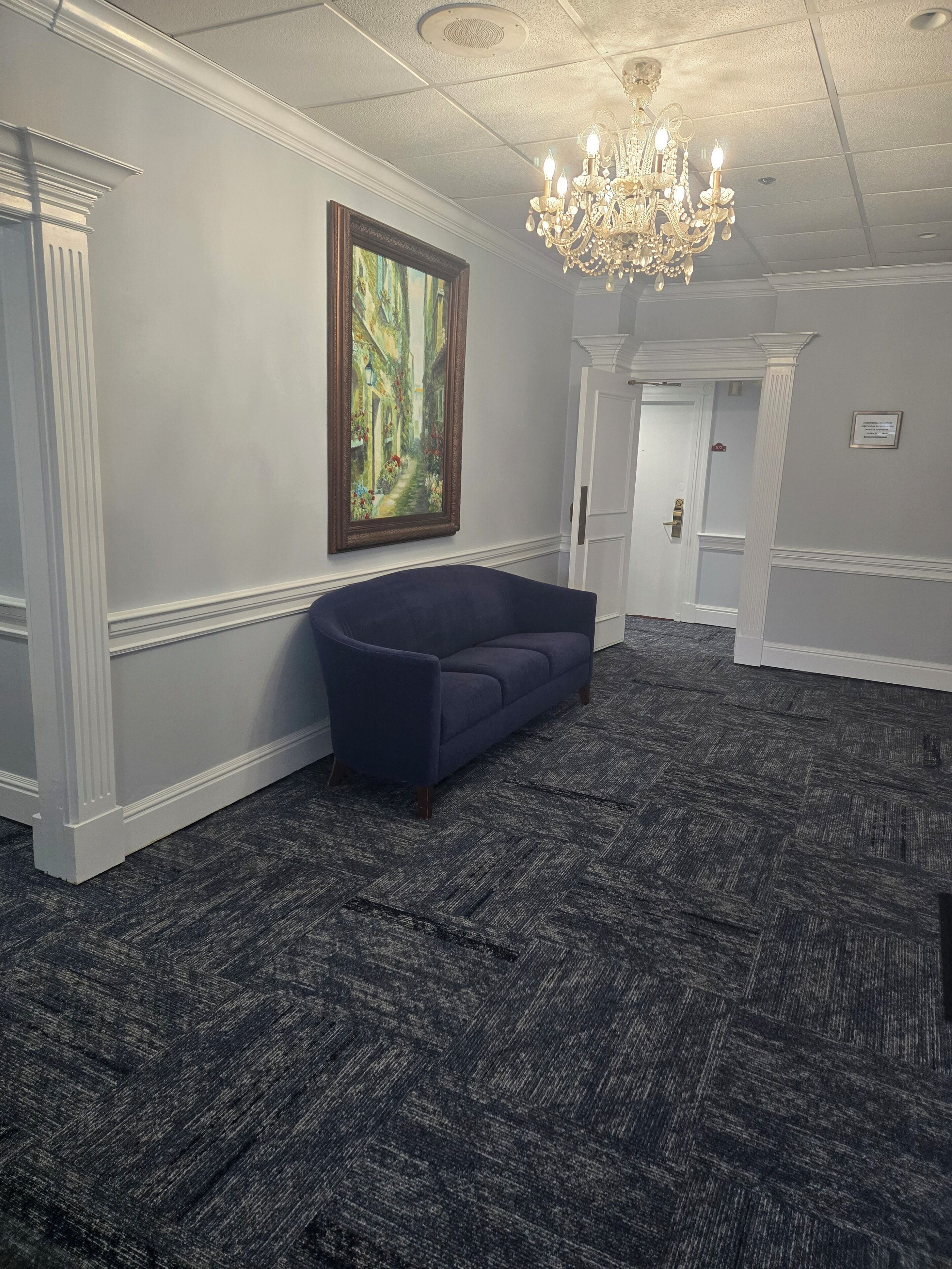 Um quarto com um sofá azul escuro, um candelabro e uma pintura na parede.