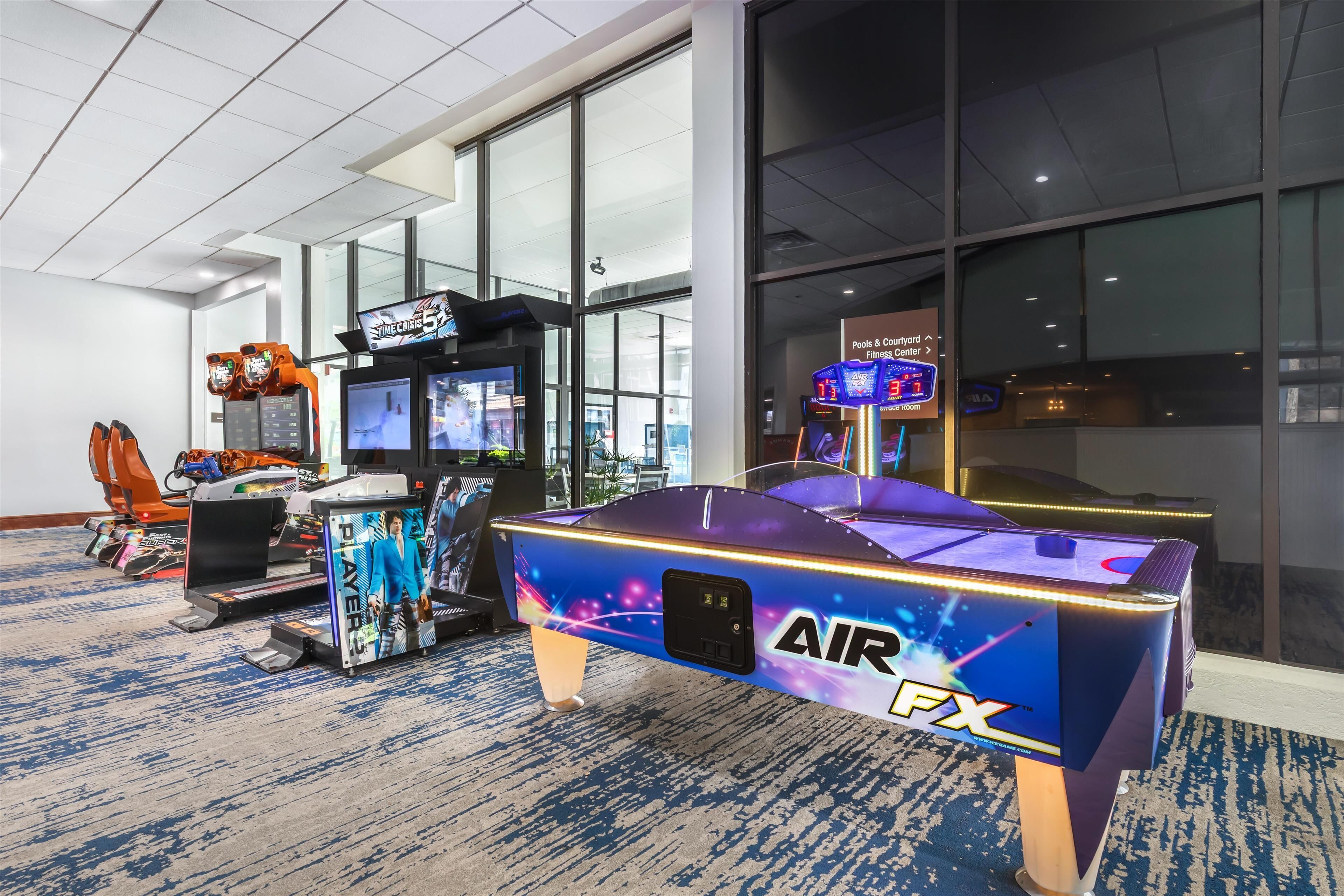 Uma mesa de bilhar com a marca 'AIR FX', uma mesa de bilhar e uma mesa de pingue-pongue em um espaço com grandes janelas e piso coberto de carpete.