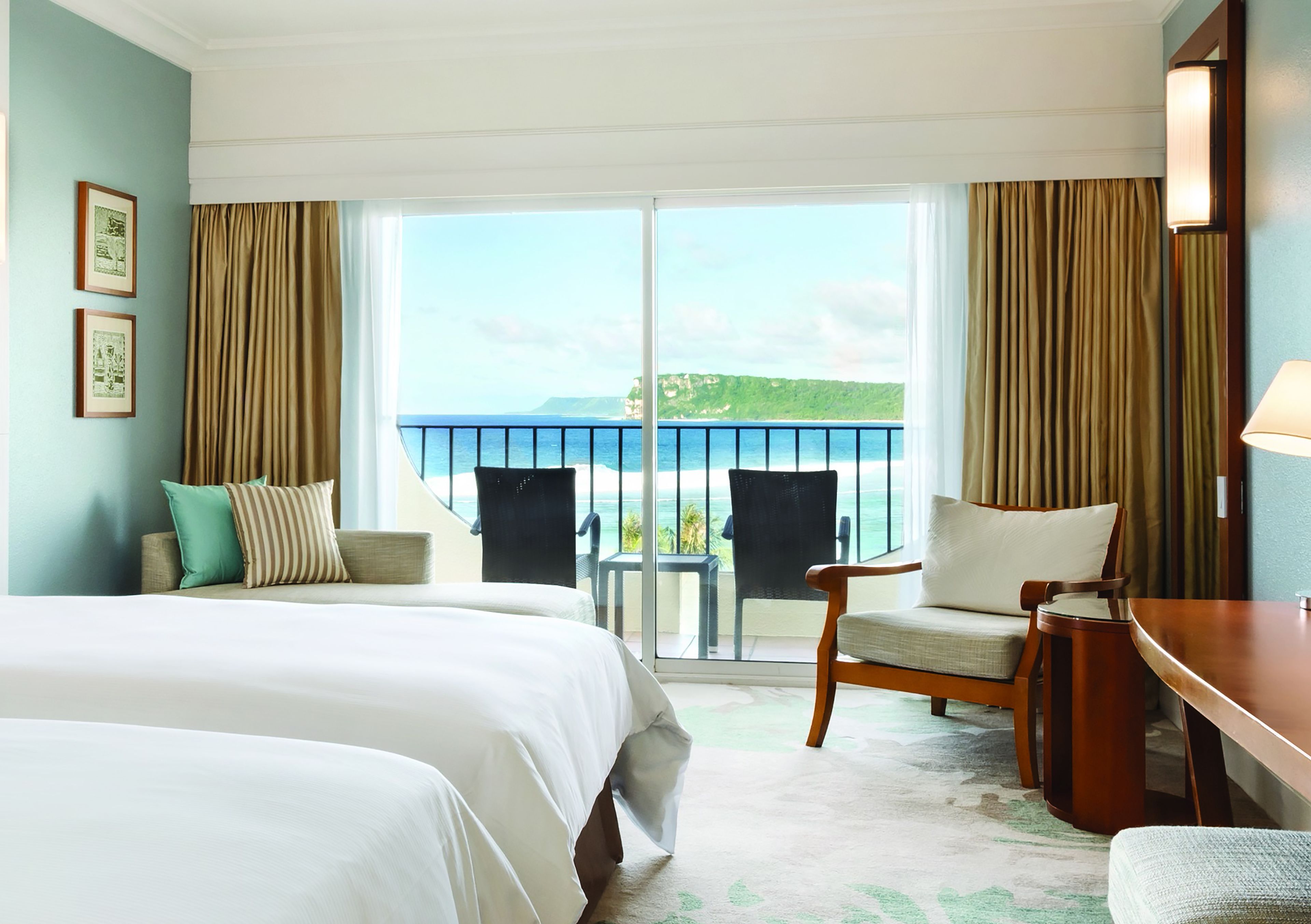 Quarto de hotel com uma cama grande, duas poltronas, uma mesa pequena e varanda com vista para o mar.