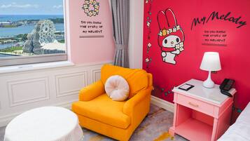 Quarto com vista para um horizonte costeiro, parede rosa com um personagem de desenho animado, poltrona amarela, mesa branca e mesa de cabeceira rosa.