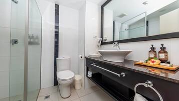 Uma casa de banho moderna com cabine de duche em vidro, sanita branca, toucador com lavatório e espelho.