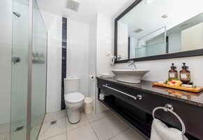 Uma casa de banho moderna com cabine de duche em vidro, sanita branca, toucador com lavatório e espelho.