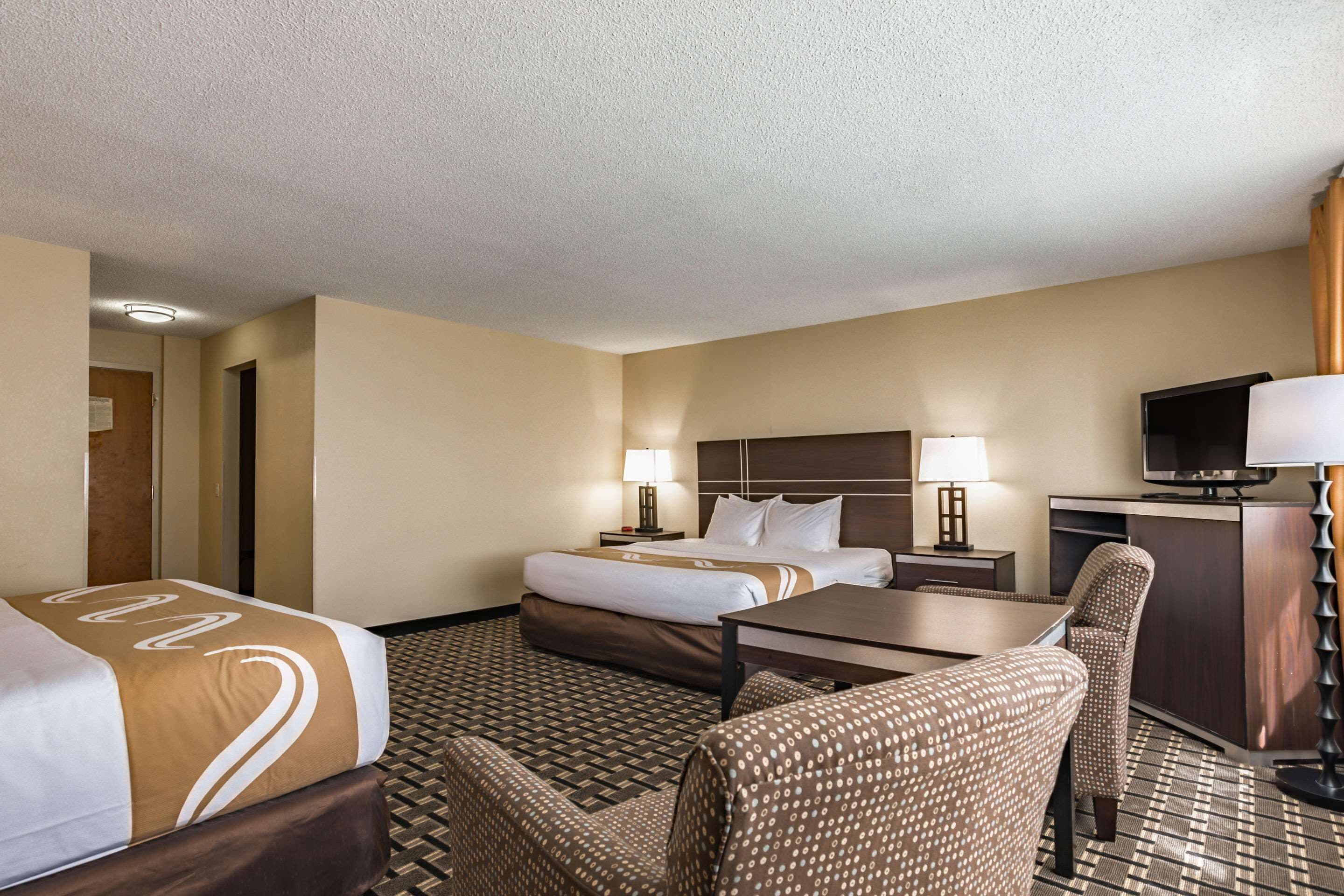 Quarto de hotel com duas camas, uma escrivaninha, uma cadeira, uma televisão e uma luminária.