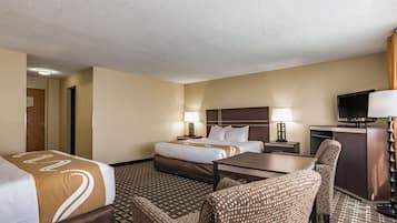 Quarto de hotel com duas camas, uma escrivaninha, uma cadeira, uma televisão e uma luminária.