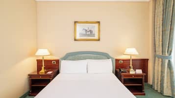 Quarto de hotel com uma cama grande, duas mesas de cabeceira com luminárias, um quadro na parede e uma janela com cortinas.