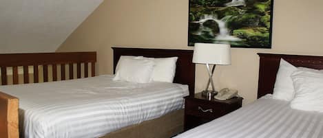 Quarto de hotel com duas camas, mesa de cabeceira com abajur e quadro de uma cachoeira na parede.