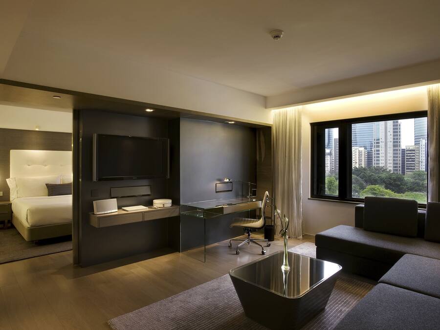 Quarto de hotel moderno com cama, escrivaninha, televisão, sofá e vista da cidade.