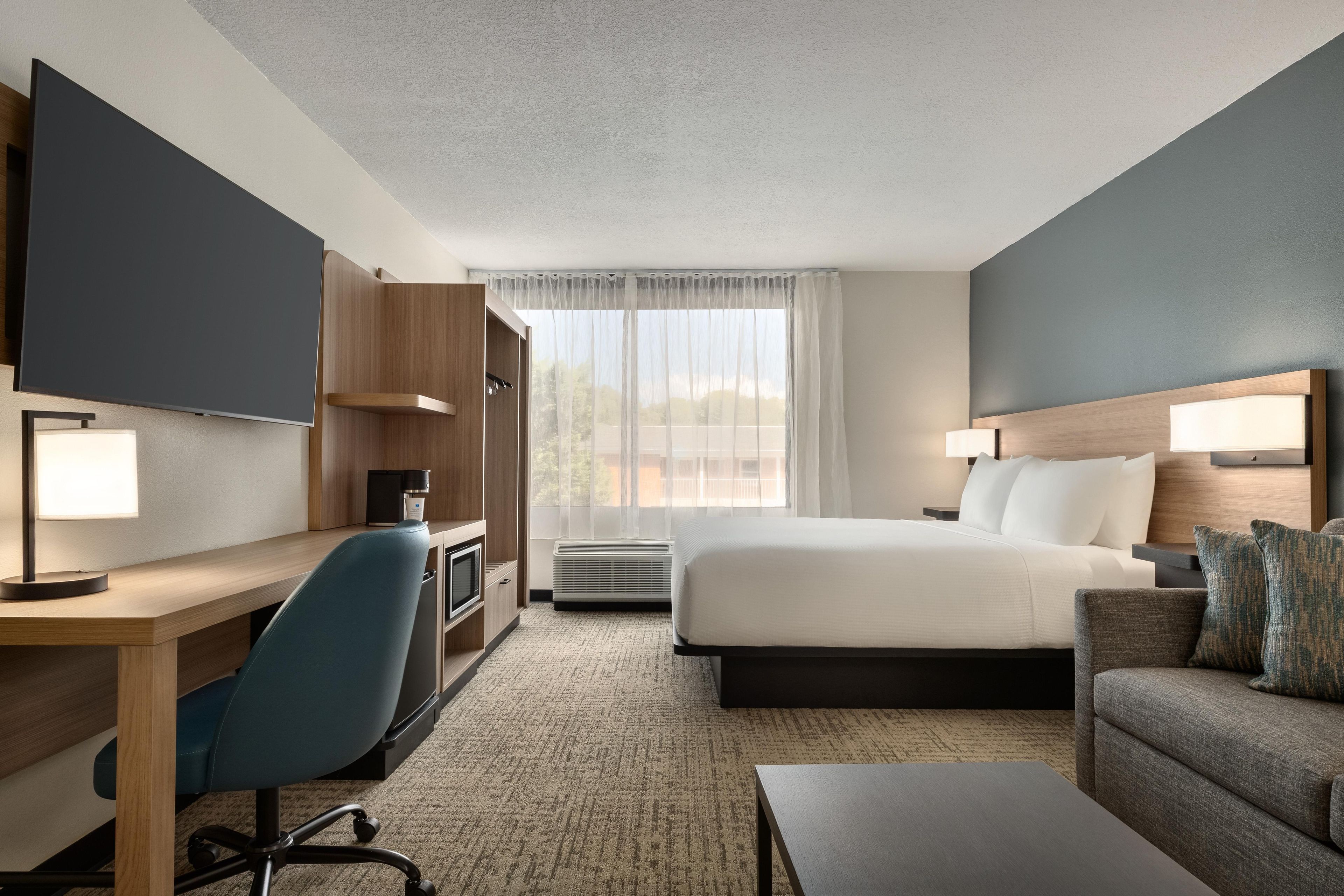 Quarto de hotel com cama, escrivaninha, cadeira, televisão e vista para o exterior.